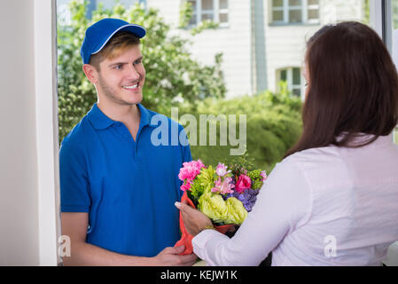 Young delivery man with bouquet of beautiful flowers on yellow ...