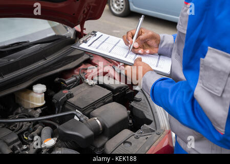 Car mechanic checking a car engine and writing on clipboard; panoramic ...