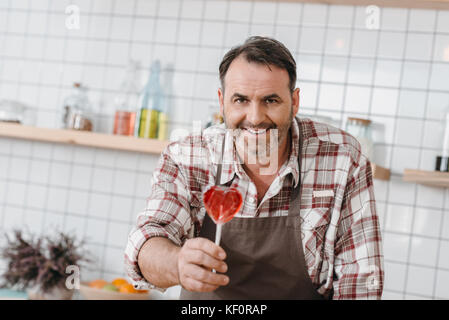Happy man in red apron and toque giving OK holding cooks knife yellow ...