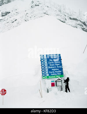 CANADA, person standing shoveling snow from around sign, Fernie Ski ...