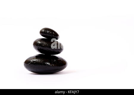 Three wet, black stones stacked in balance on a misty beach with smooth pebbles background Stock ...