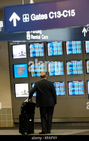Passengers looking at flight information display board showing ...