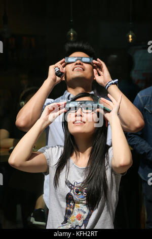 Man and woman watch the solar eclipse begin using protective glasses ...