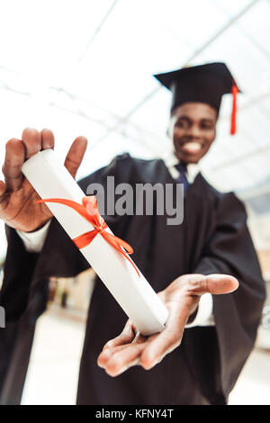 Happy graduated man in a black gown jumping while holding his diploma ...