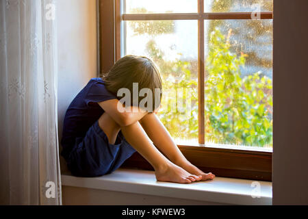 Sad boy sitting near window Stock Photo - Alamy