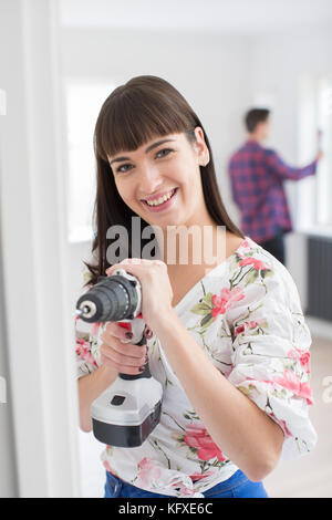 Couple renovating together as woman using power drill on wall with man ...