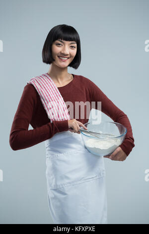 Portrait of beautiful woman chef mixing in a bowl against gray ...