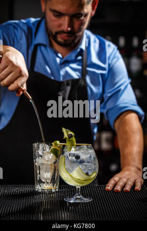 Pouring gin tonic drink into a glass on black background Stock Photo - Alamy