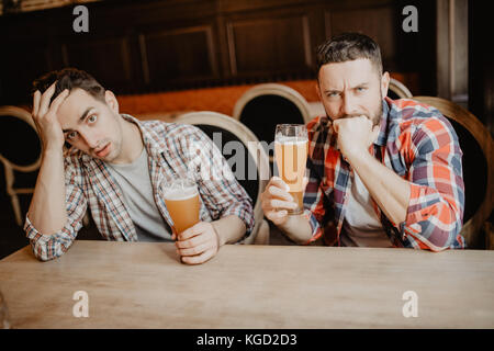 sad and depressed guy having a beer in a pub, sitting alone at a table ...