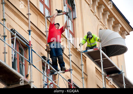 Two men putting up scaffolding without any kind of safety equipment ...