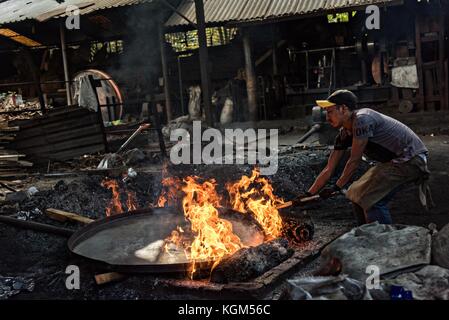 An indigenous Purepecha worker works a copper pan on an open forge to ...