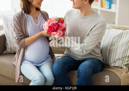 Young man greeting his wife with bouquet of flowers at home on ...