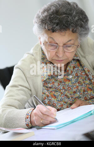Senior woman sitting and filling up documents at kitchen table Stock ...
