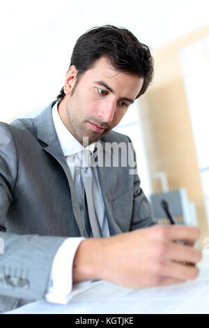 Businessman signing contract or application form leaning on his office ...