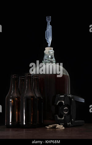 Fermented beer in a demijohn with airlock and hand capper with dark ...