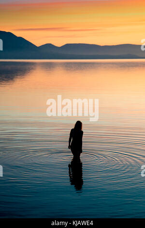 A lone woman bather is reflected as she enters the calm water of the ...