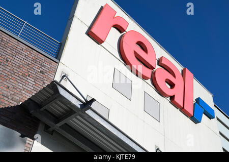 A logo sign outside of a Real (real,-) hypermarket retail store in ...
