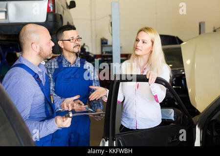A tired sad caucasian woman mechanic is sitting leaning on a car in an ...