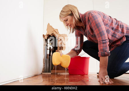 Woman mopping up water from a burst pipe with sponge, vertical Stock ...