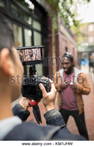 Man with video camera vlogging, videoing friend talking and drinking ...