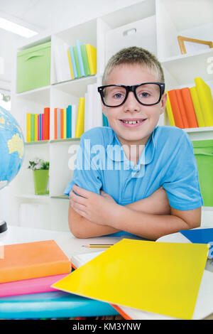 Smiling intelligent boy holding pile of books while standing in modern ...