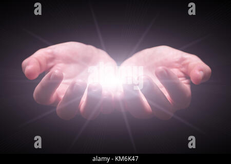 Two hands hold a glowing light or sun as symbol for meditation or pray ...
