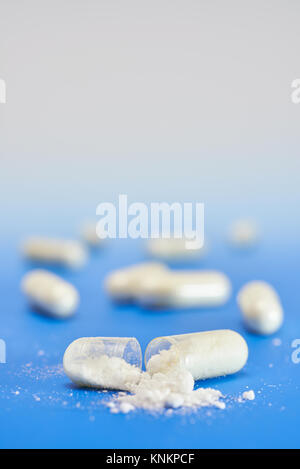 Split-open transparent capsule with white powder on blue gradient ...