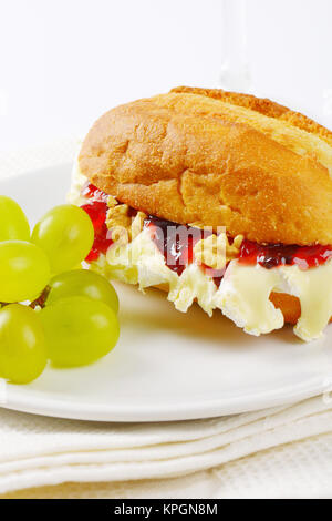 small baguette with brie cheese, walnuts, jam and grapes on white plate ...