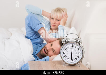 unhappy couple being awakened by an alarm clock in bedroom in the ...