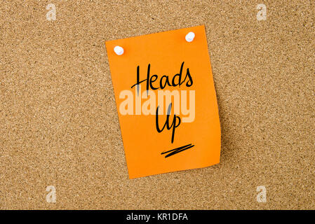 Heads Up written on orange paper note pinned on cork board with white ...