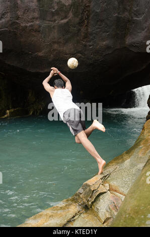 Back view of a boy diving off cliff, throwing away a ball, falling ...