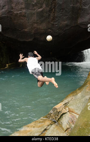 Back view of a boy diving off cliff, throwing away a ball, falling ...