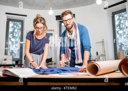 Couple of fashion designers working with fabric at the studio full of ...