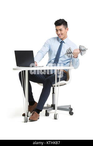 Young businessman lifting weights while using computer at work Stock ...