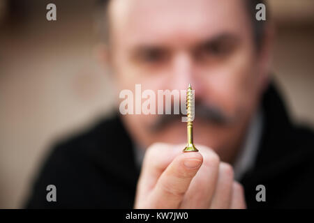 Man holding a screw on his finger and looking at it Stock Photo - Alamy