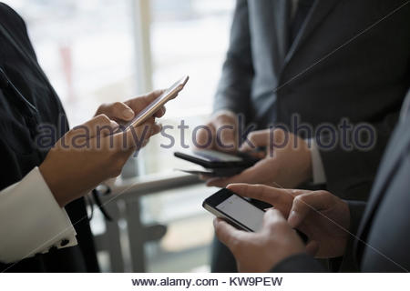 Business people texting with cell phones in sunny conference room ...