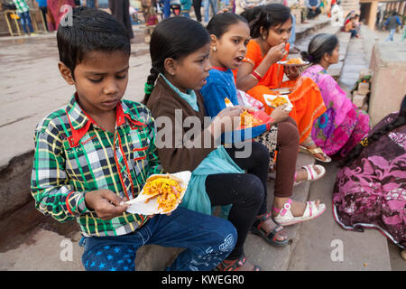 Children eat a snack of bhel puri on the ghats at Varanasi in India ...