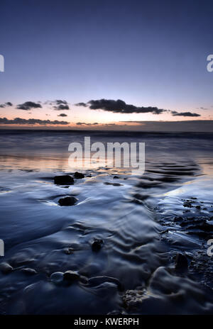 Sunset on a serene beach with rippled sand and silhouetted trees in the ...