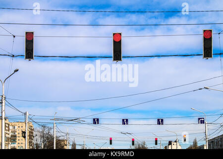 Three red traffic lights hang over the road against the blue sky ...