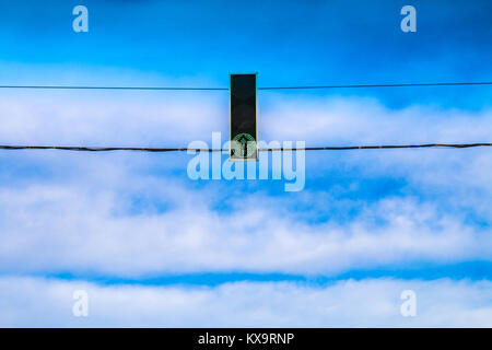Three red traffic lights hang over the road against the blue sky ...