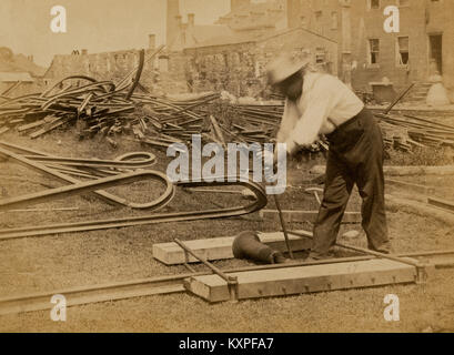 Railroad construction worker straightening track; pile of twisted rails ...