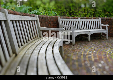 Traditional wooden curved park seat in a shady corner surrounded by ...