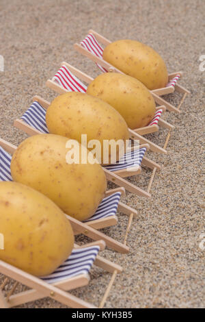 New potatoes on toy deckchairs on sand - as visual metaphor for concept ...