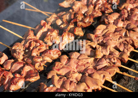 Street food vendor grilling skewered sausages and burgers at a market ...