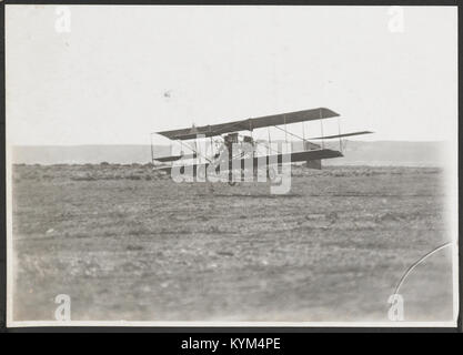 A photograph of a Curtiss Pusher biplane in flight over an airfield ...