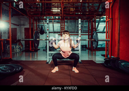 Gorgeous young fitness woman crouch and doing squad exercise with a bar ...