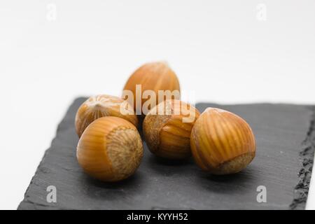 Several whole hazelnuts on small black slate board. Isolated on white ...