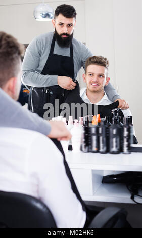 Man making client comfortable before haircut at salon Stock Photo - Alamy