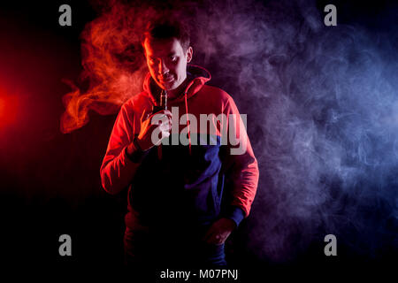 Man in sport hoody vaping an electronic cigarette.Isolated on black ...
