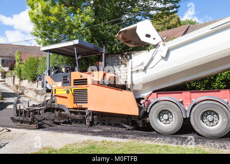 Road tarring machine and tip truck tarring a narrow rural village ...